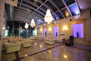 Um hall amplo com assentos confortáveis, lustres e grandes janelas com iluminação roxa.