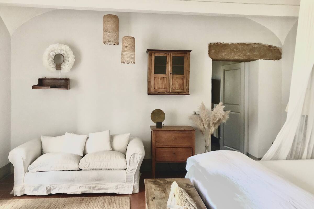 Um quarto com um sofá branco, um armário de madeira, uma cama e uma porta com cortina.