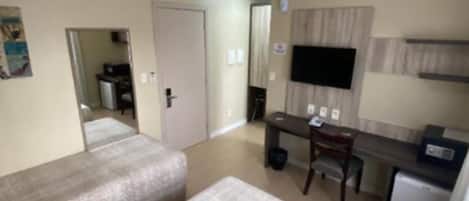 Quarto de hotel com duas camas, uma escrivaninha com cadeira, uma kitchenette compacta, uma televisão de ecrã plano na parede e um espelho.
