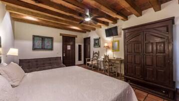 Quarto com cama grande, vigas de madeira no teto, escrivaninha com cadeiras e guarda-roupa.