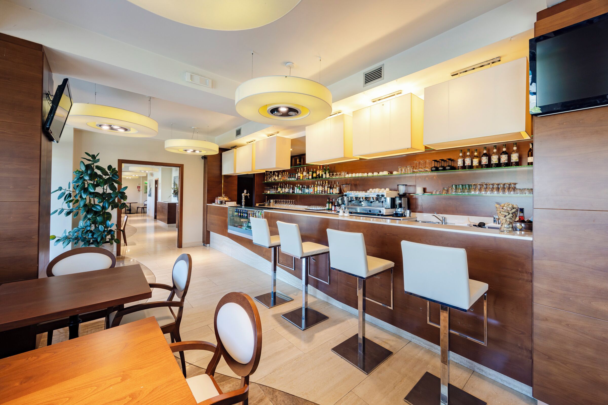 Uma área de bar moderna com um balcão longo, vários bancos altos e uma variedade de garrafas e copos.