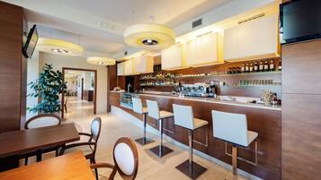 Uma área de bar moderna com um balcão longo, vários bancos altos e uma variedade de garrafas e copos.