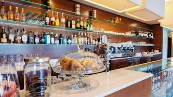 Uma área de bar com prateleiras de garrafas de bebidas e copos, uma máquina de café e uma vitrine de doces.