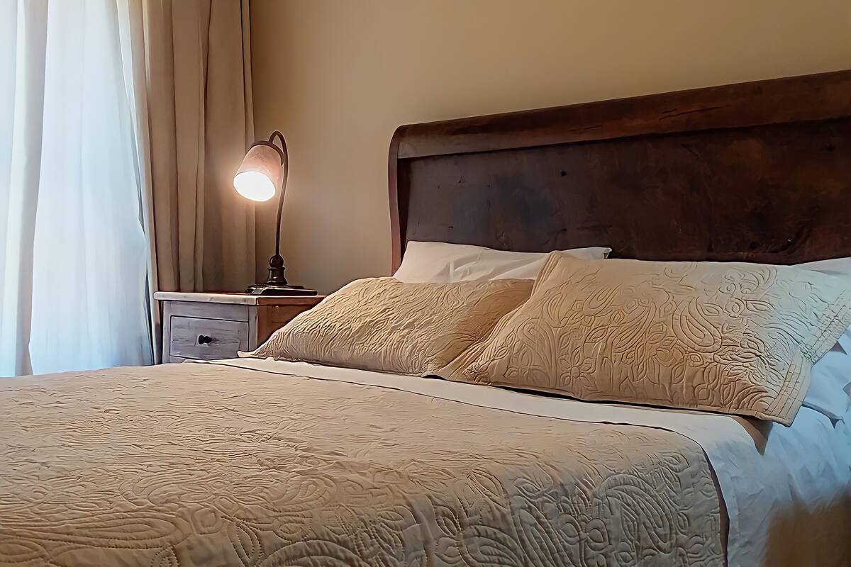 Cama bem arrumada com colcha texturizada, cabeceira de madeira e abajur.