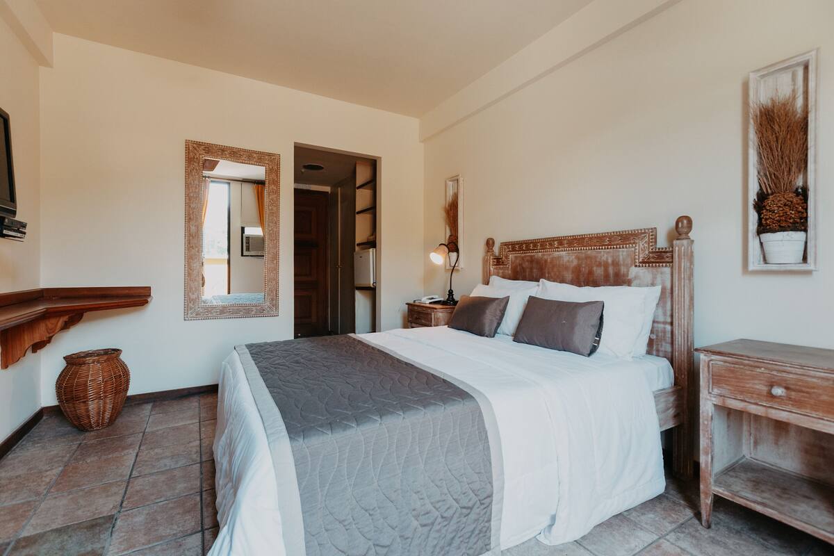Quarto com cama, mesa de cabeceira, espelho e planta em vaso.