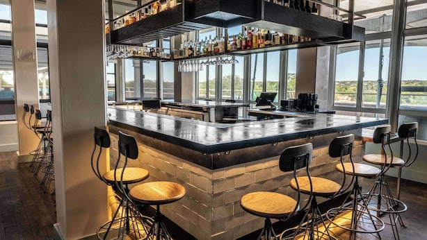 Uma área de bar com balcão alto, banquetas e diversas garrafas e copos.
