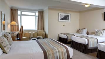 Quarto de hotel com duas camas, uma escrivaninha, uma cadeira e uma janela com cortinas.