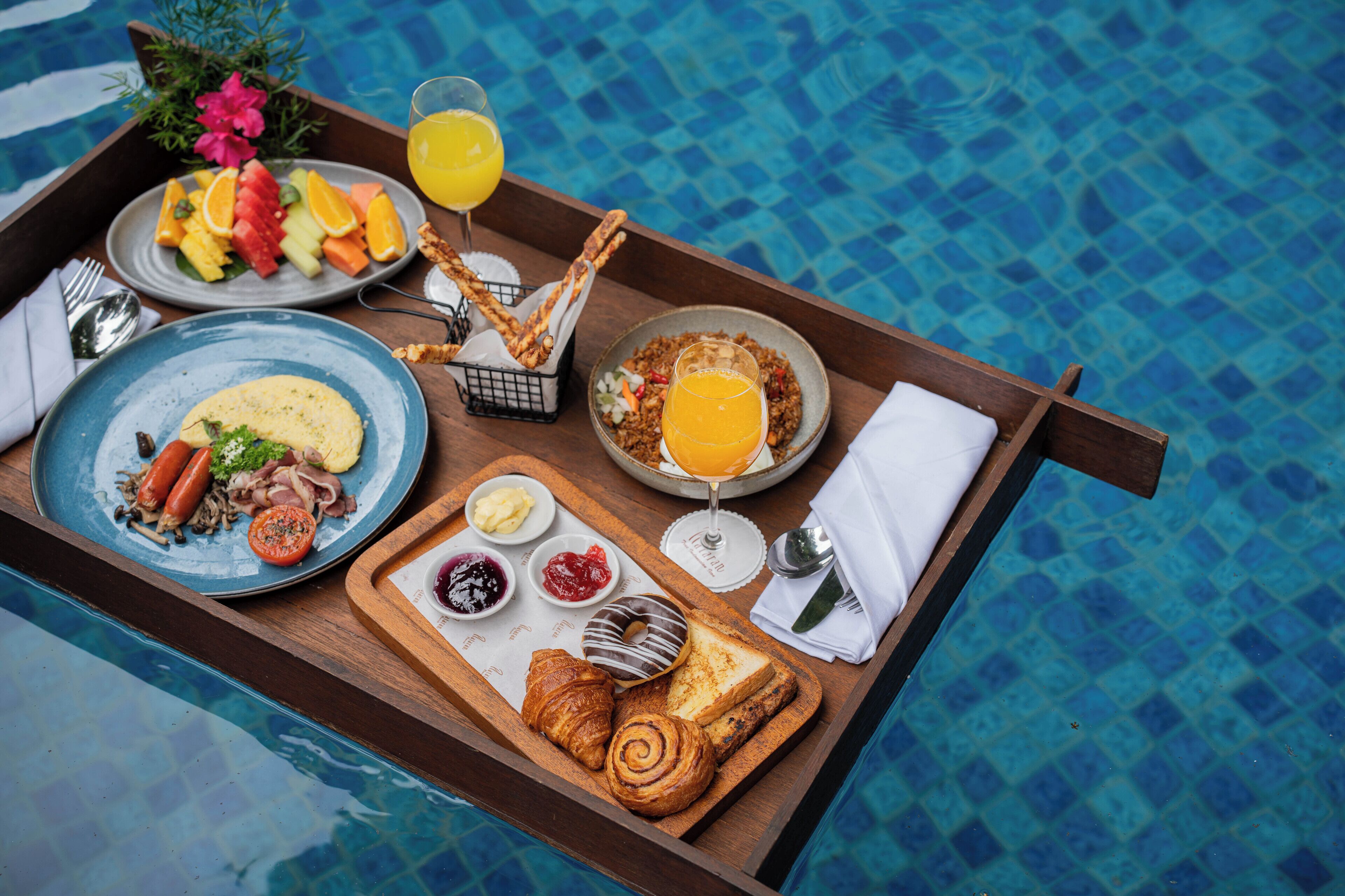 Bandeja de café da manhã com diversos alimentos e bebidas à beira de uma piscina.