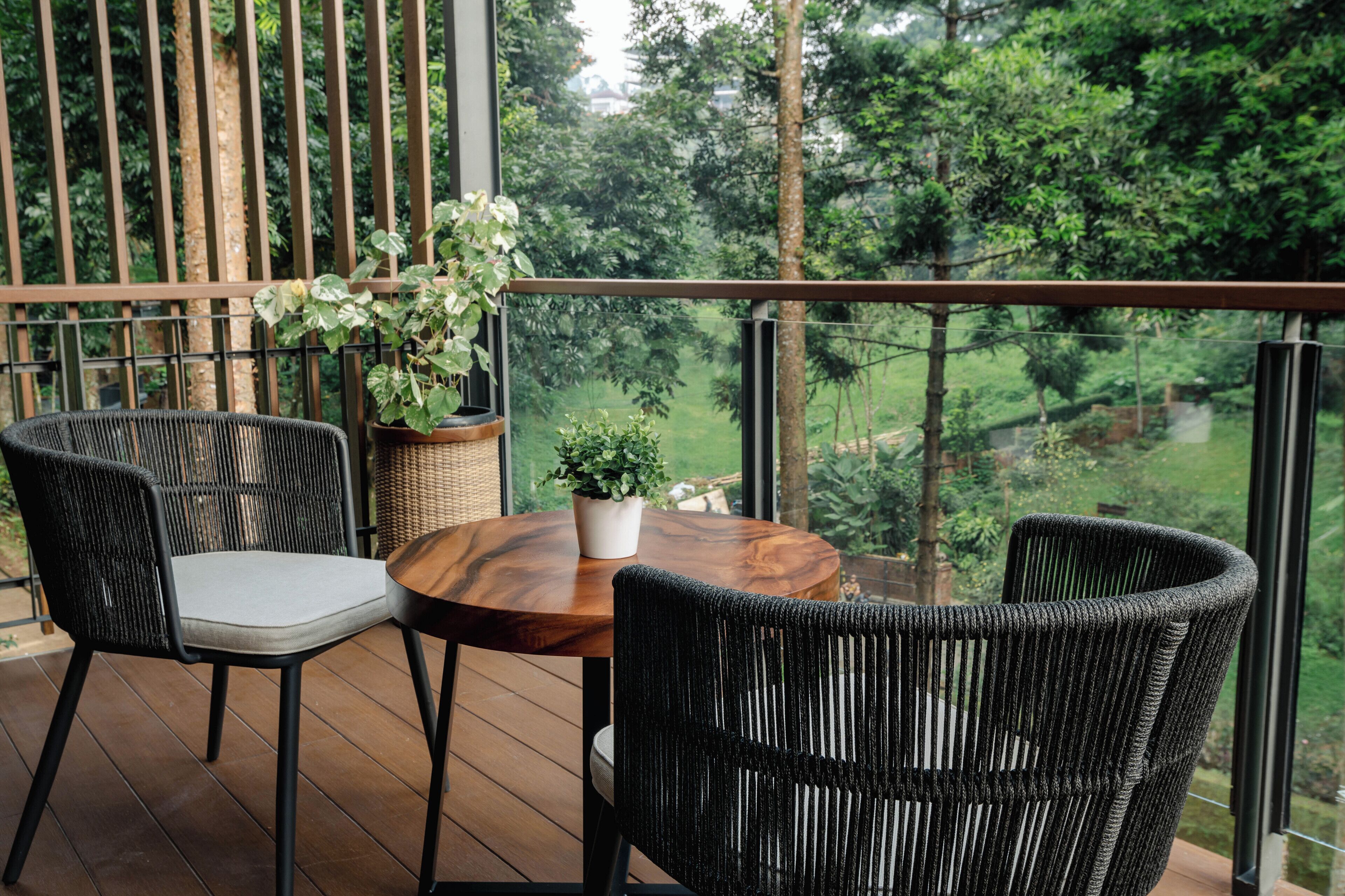 Varanda com cadeiras de vime, uma mesa de madeira e um vaso com planta.
