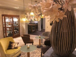 Uma sala de estar moderna com um sofá amarelo, uma poltrona marrom, um vaso listrado grande e uma mesa de vidro com uma vela.