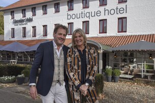 Um hotel boutique com fachada branca, telhado de telhas vermelhas e área de estar externa com guarda-sóis.
