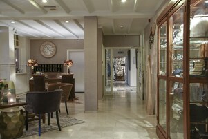 Um saguão de hotel com área de refeições, um relógio grande e uma vitrine com diversos objetos.