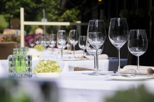 Uma mesa posta para refeição, com copos transparentes e uma pequena tigela com enfeite verde.
