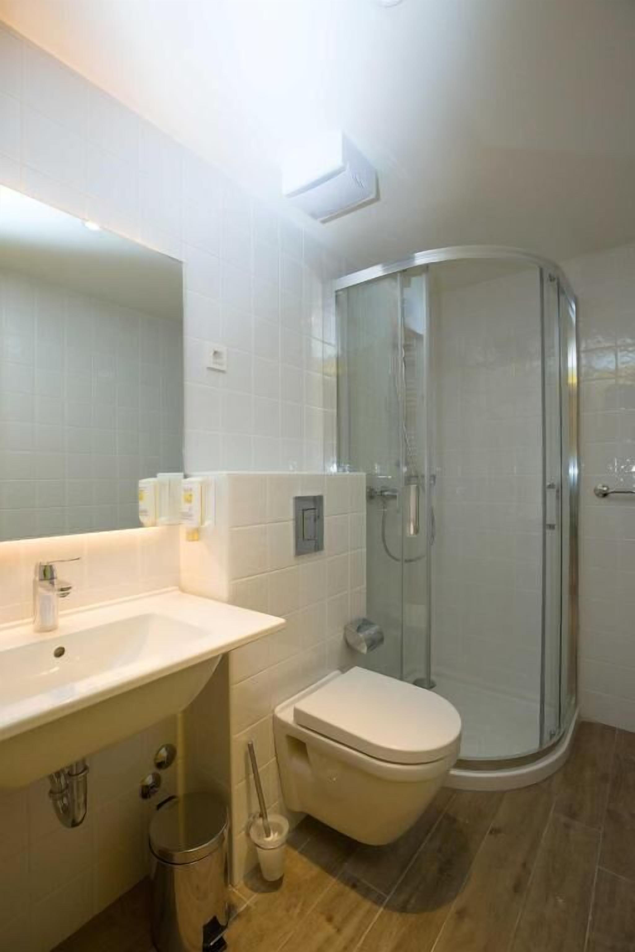Casa de banho moderna com cabine de chuveiro em vidro, lavatório branco e sanita.