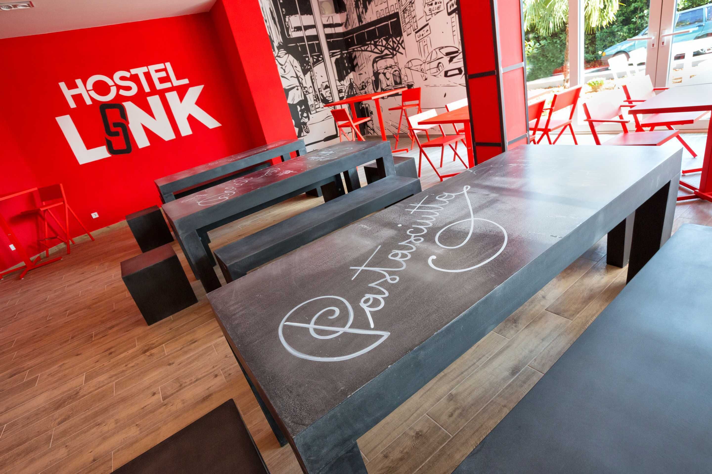 Interior de um hostel com parede vermelha, um mural em estilo de graffiti e uma mesa com a palavra 'Pantsy'.