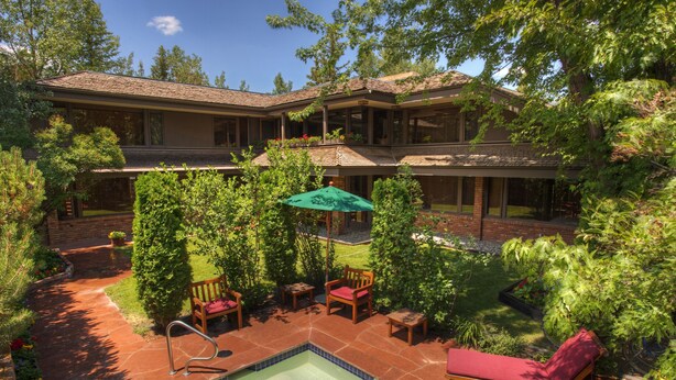 Uma casa de dois andares com piscina, móveis de varanda e vegetação exuberante.