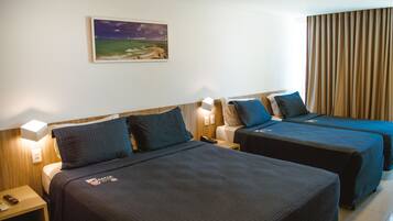 Quarto de hotel com duas camas, uma mesa de cabeceira, um quadro de uma praia e uma cortina.