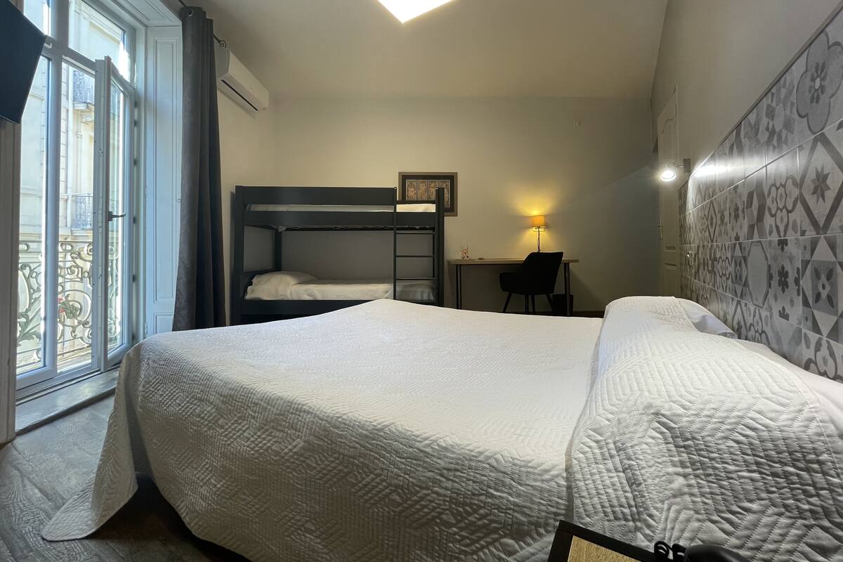 Quarto com uma cama de solteiro, uma escrivaninha com cadeira, uma luminária e uma janela com cortinas.
