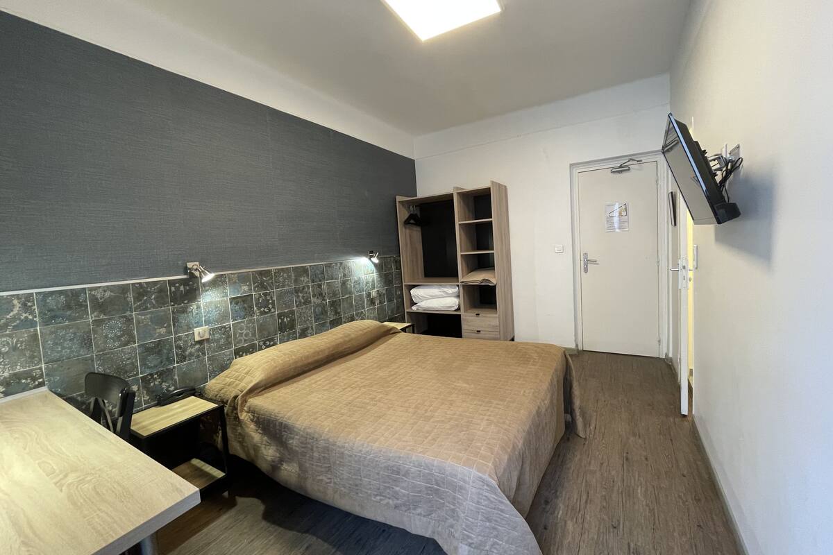 Quarto de hotel pequeno com cama, uma secretária, um guarda-roupa e uma porta.