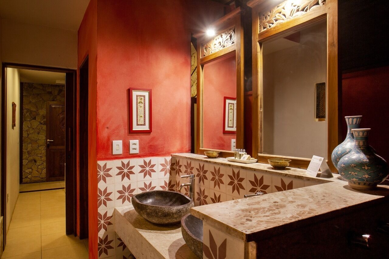 Casa de banho com um espelho grande, uma bacia de pedra e um vaso decorativo.