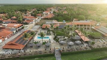 Resort com vários edifícios, piscina e palmeiras.