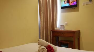 Quarto de hotel com cama, televisão fixada na parede, mesa de cabeceira de madeira e janela com cortinas.