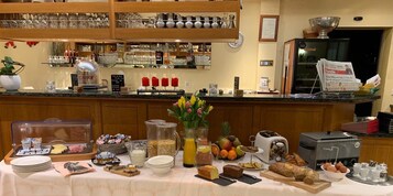 Buffet montado com diversos alimentos, uma máquina de café e um suporte para jornais.