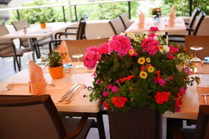 Uma mesa de jantar posta com um arranjo de flores coloridas, talheres alinhados e um vaso de planta.