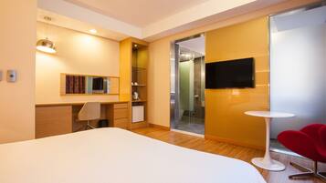 Quarto de hotel moderno com uma cama grande, uma escrivaninha com cadeira, TV na parede e uma cadeira vermelha.