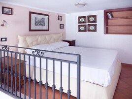 Quarto com cama, mesa de cabeceira, prateleira na parede e escada.