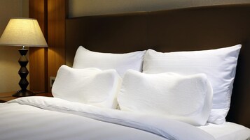 Cama bem arrumada com lençóis e almofadas brancos, cabeceira de madeira e abajur em uma mesa de cabeceira.