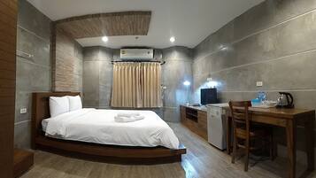 Quarto de hotel compacto com uma cama, escrivaninha, cadeira, pequeno frigorífico e ar condicionado.