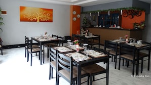 Um restaurante com várias mesas e cadeiras, uma área de bar e um teto com iluminação embutida.
