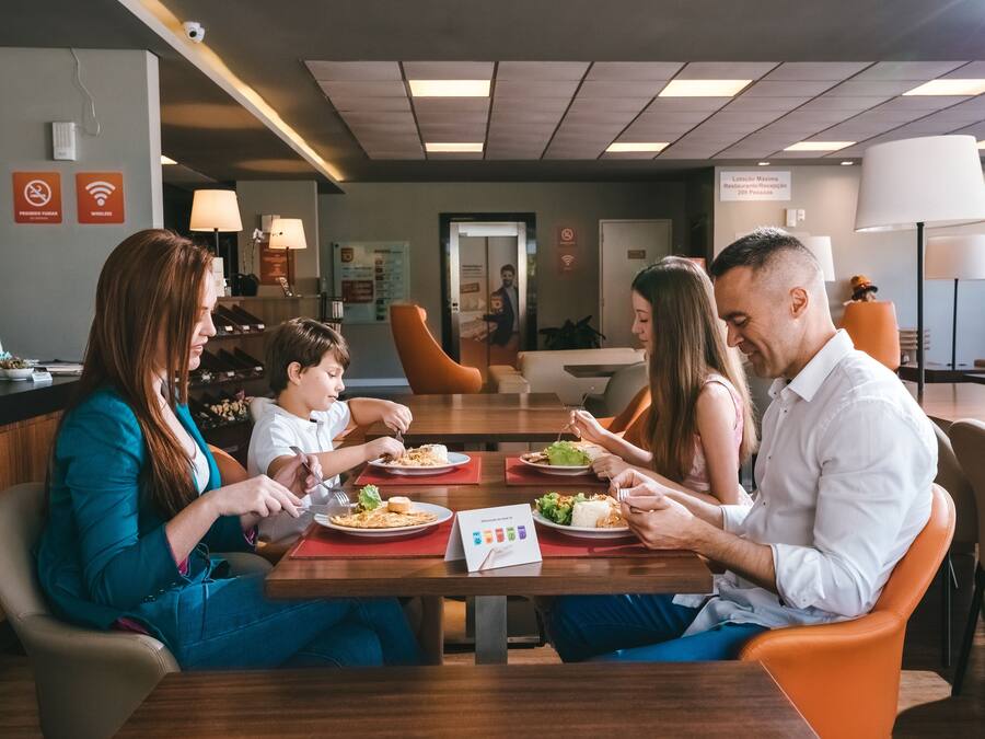 Um grupo de pessoas jantando em um restaurante com decoração moderna, incluindo uma mesa de madeira, cadeiras e um cardápio.