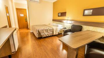 Quarto de hotel com cama, mesa de cabeceira, cadeira e escrivaninha.