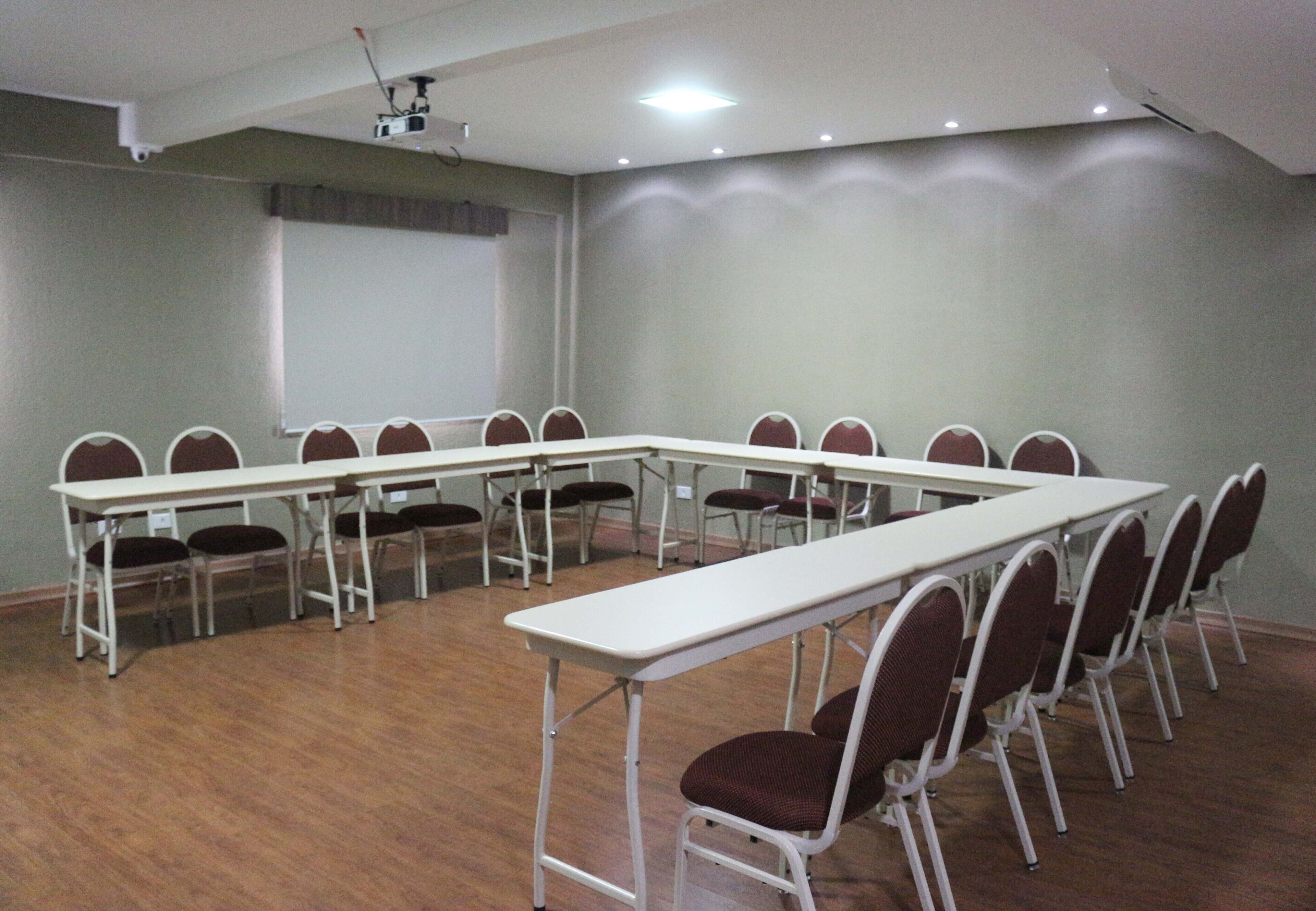 Uma sala de conferência com uma mesa comprida e cadeiras, uma tela de projetor e um quadro branco.