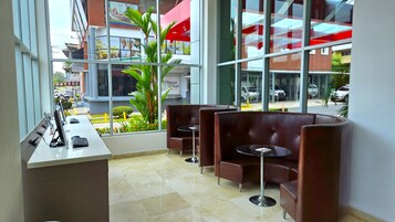 Interior moderno com balcão de recepção, área de estar e amplas janelas que oferecem vista da rua e edifícios.