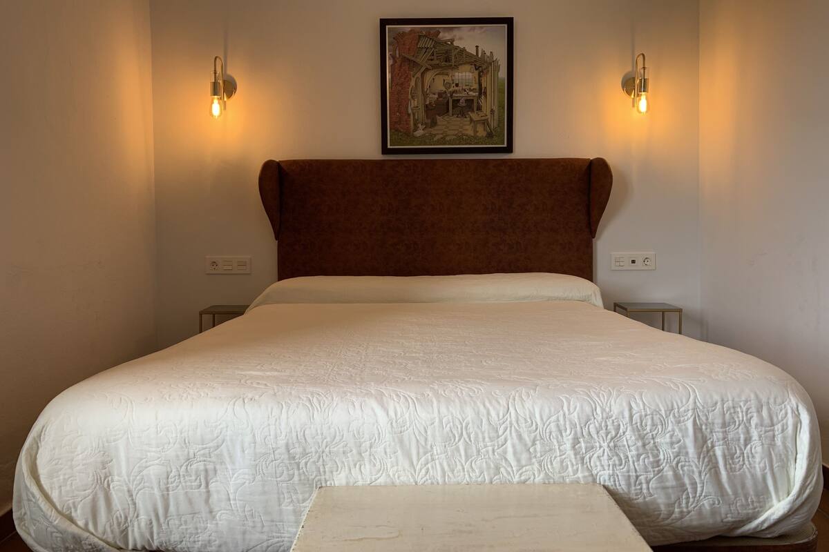 Quarto com uma cama grande, duas luminárias fixadas na parede e um quadro emoldurado sobre a cama.