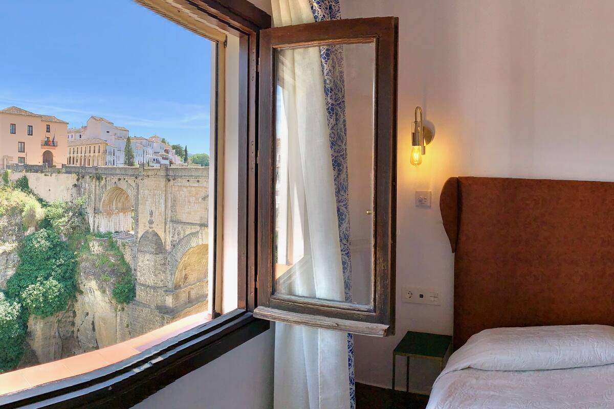 Quarto de hotel com uma grande janela com vista para uma ponte de pedra histórica e edifícios.