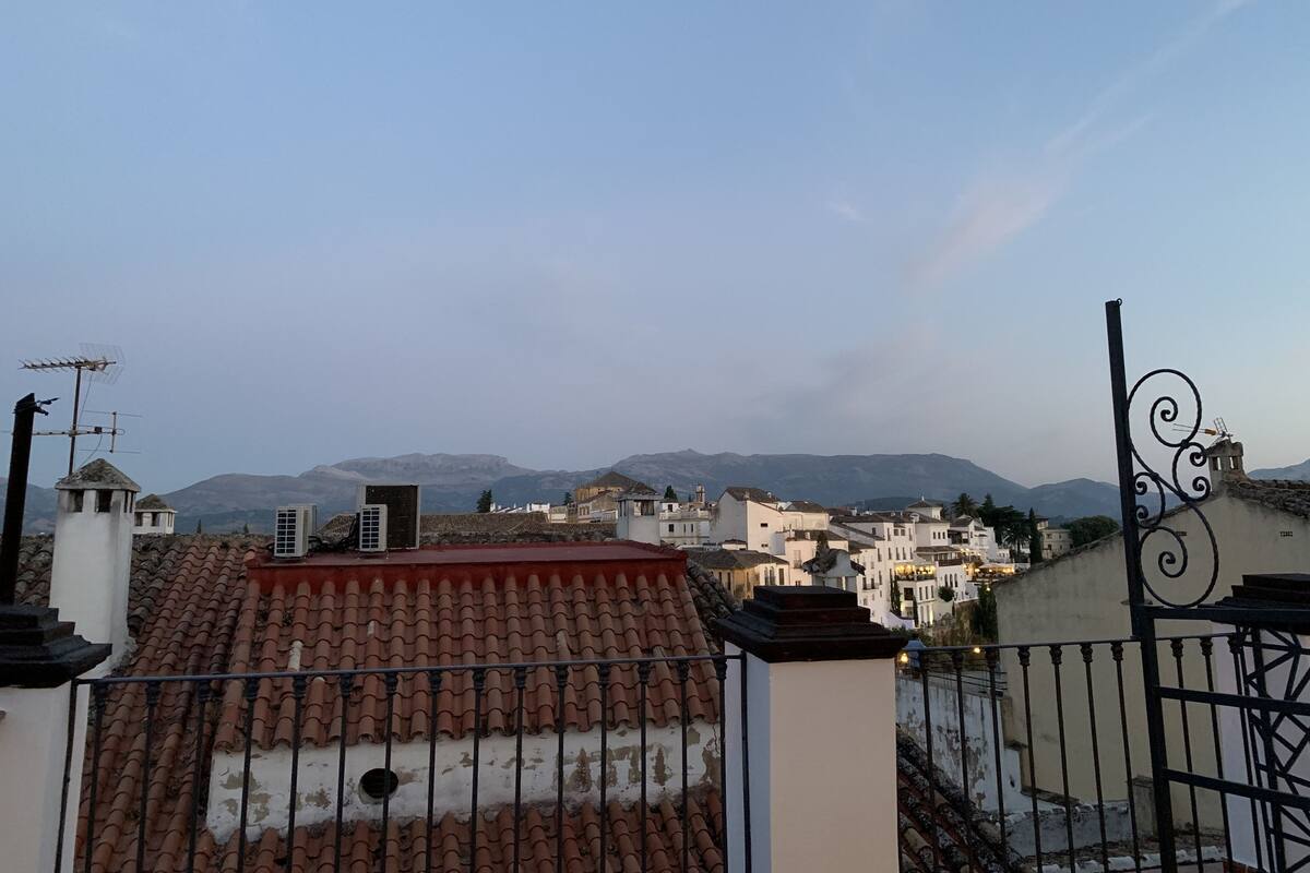 Um bairro residencial com telhados de terracota, edifícios brancos e montanhas ao fundo.