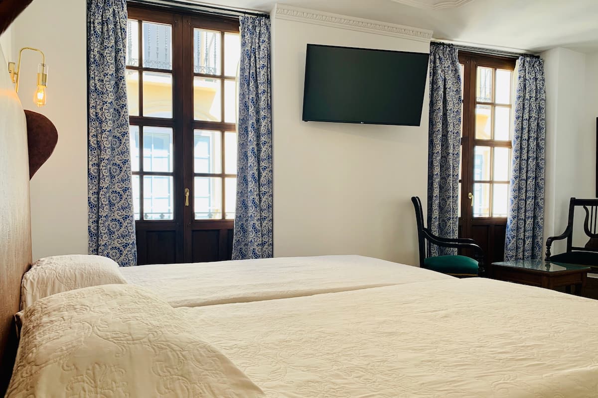 Quarto de hotel com duas camas, uma televisão de tela plana fixada na parede e janelas amplas com cortinas estampadas.