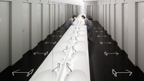 Um banheiro comprido e estreito, com várias pias e espelhos, e armários em ambos os lados.
