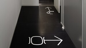 Corredor com setas indicativas no chão, uma porta com número e área de chuveiro revestida em azulejo ao fundo.