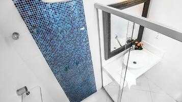 Casa de banho moderna com parede em mosaico azul, uma sanita branca e um espelho com moldura de madeira.