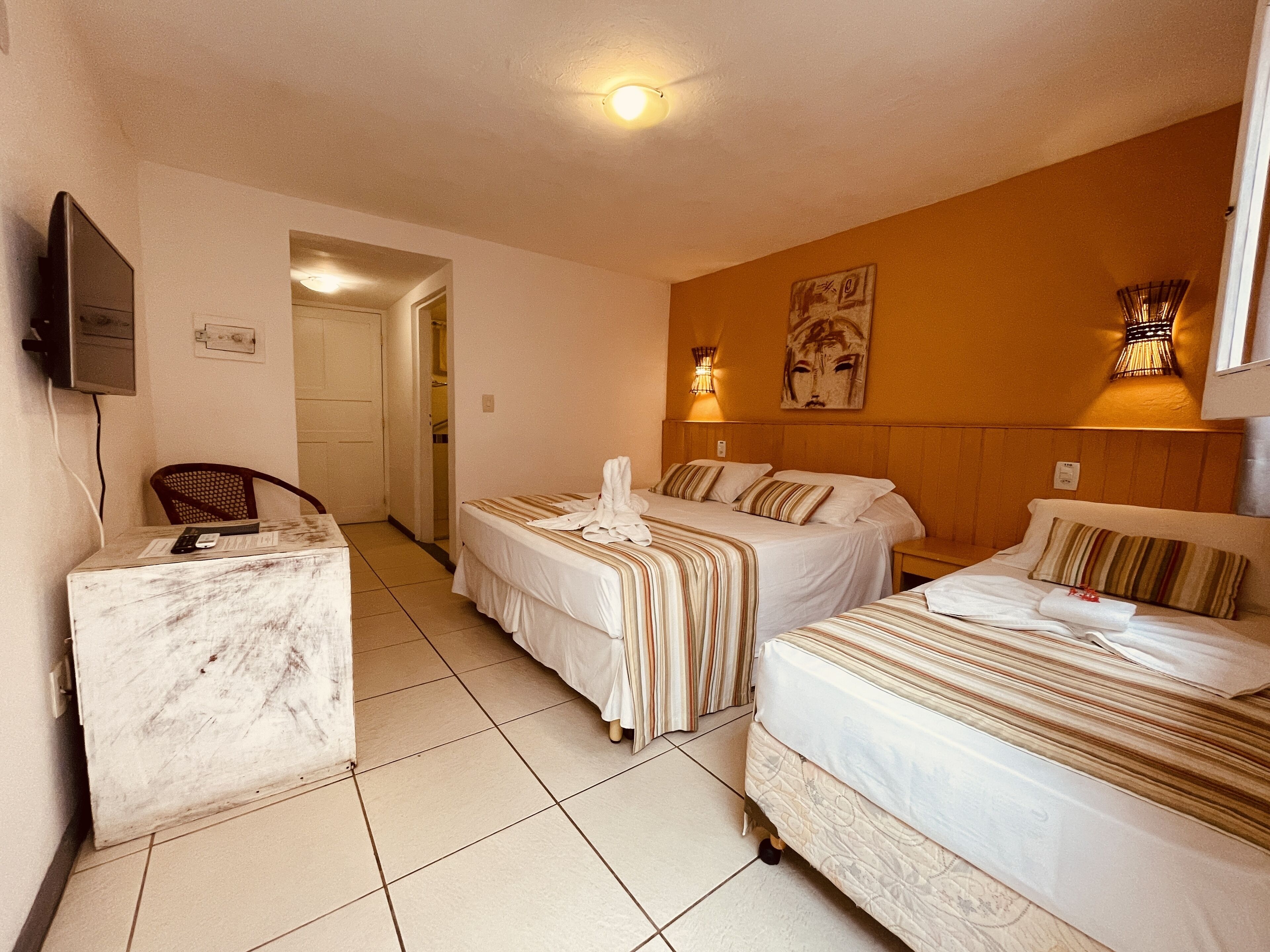 Quarto de hotel com duas camas, uma escrivaninha, uma cadeira e uma televisão.