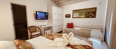 Quarto de hotel com cama, escrivaninha, televisão, guarda-roupa e banheiro visível por uma porta aberta.