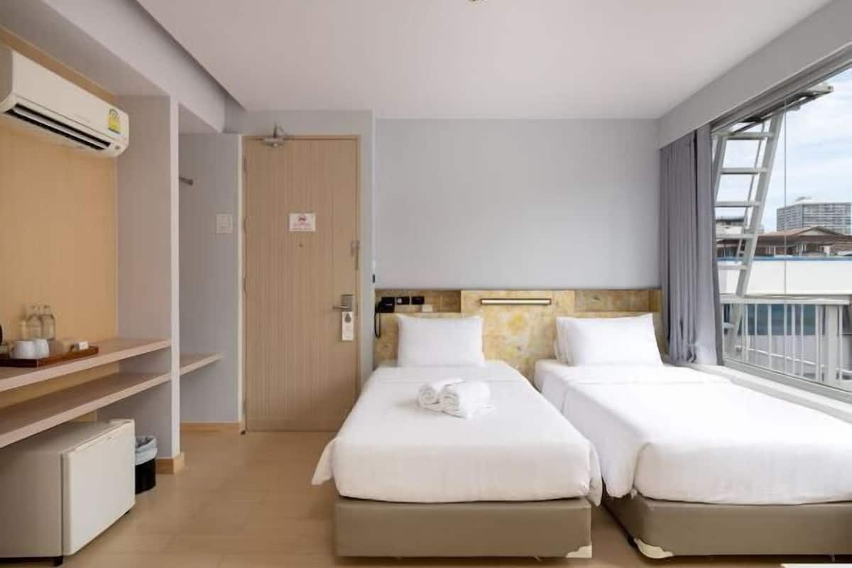 Quarto de hotel com duas camas, um minibar, uma janela com vista e uma porta para outro cômodo.