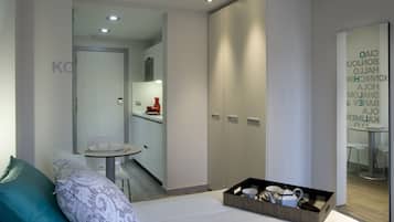 Quarto de hotel moderno com cama, uma pequena mesa e cozinha compacta.