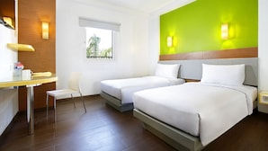 Quarto de hotel com duas camas, uma escrivaninha, uma cadeira e uma janela com vista para o verde.