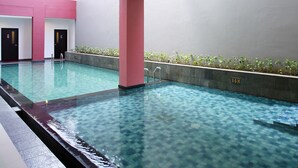 Piscina interior com água azul cristalina, rodeada por paredes com tons de rosa e cinza.